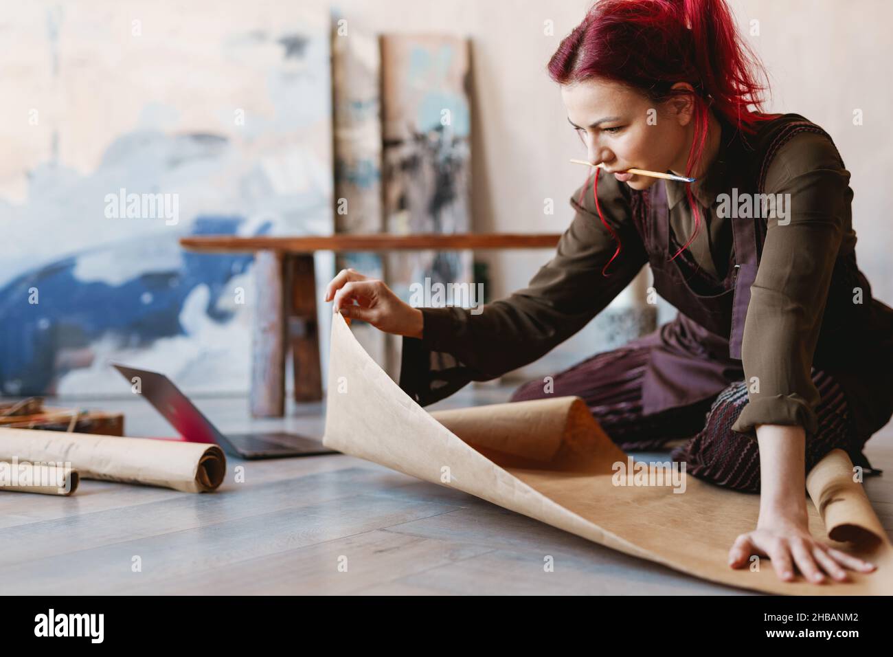 Young woman artist sitting on a floor of an art studio unrolling ...
