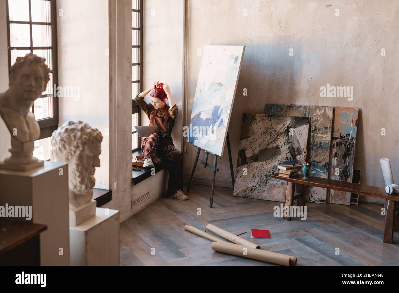 Young white woman painter in an art studio, using laptop computer for ...