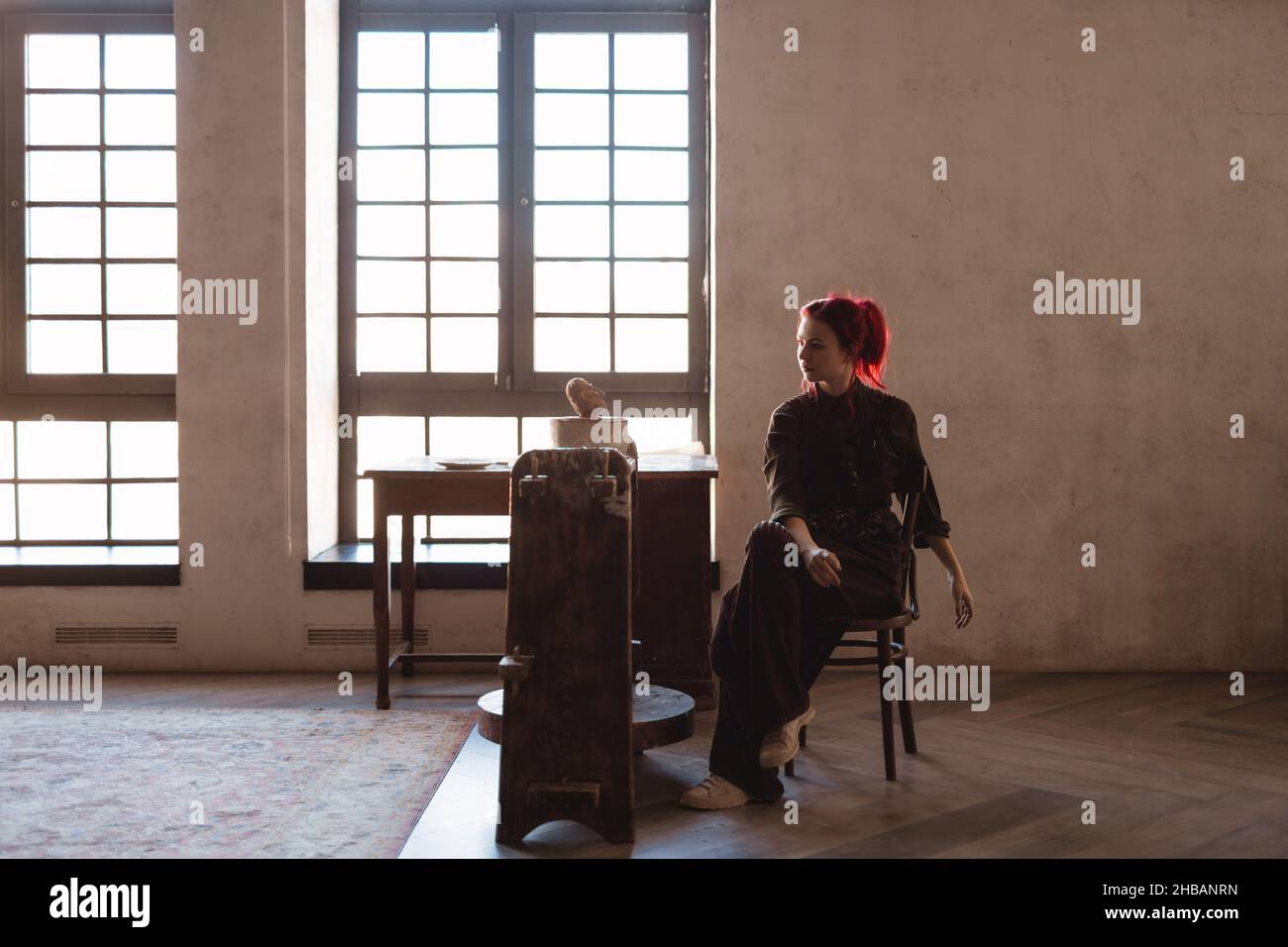 Young woman sculptor artist looking at a bust sculpture with clay in an ...