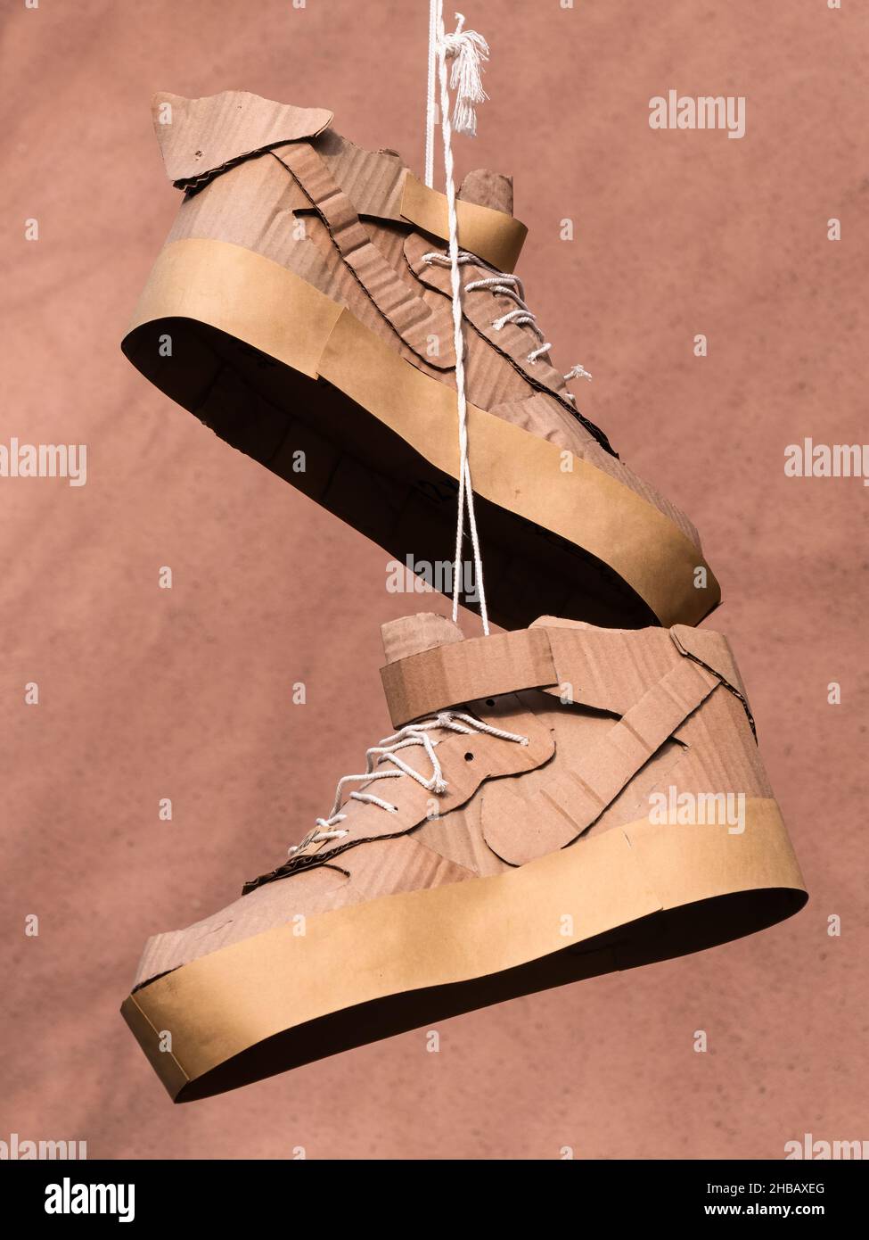 A pair of shoes made of cardboard hanging in the air on a white string ...