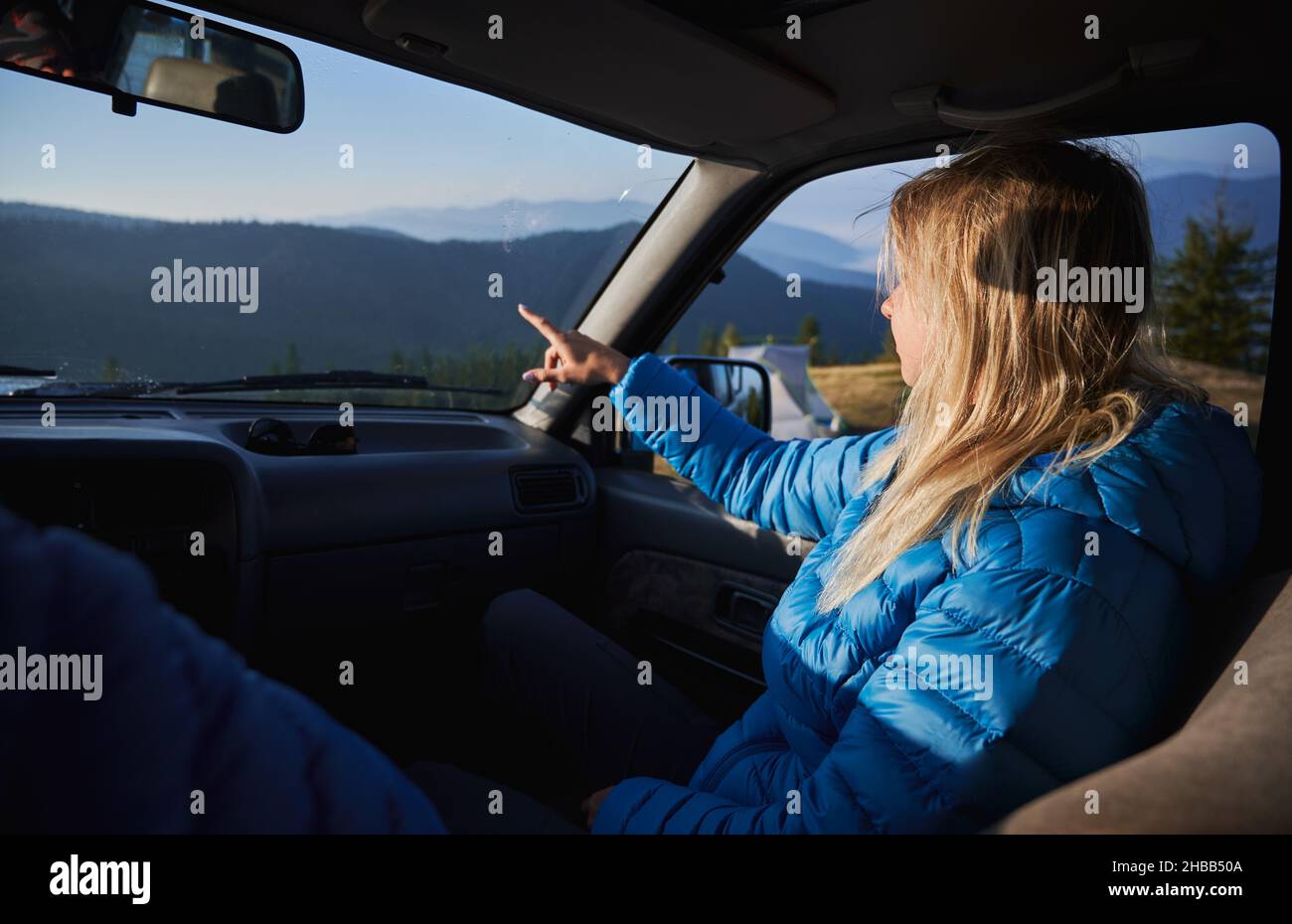 Female passenger of car pointing driver to high mountain hills in front ...