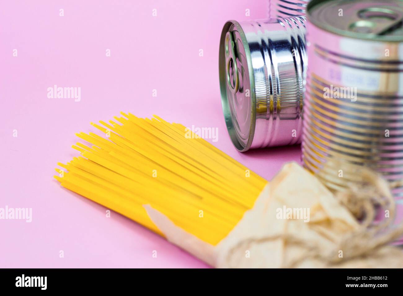 Tinned food, metal cans and yellow spaghetti pasta on pink background ...