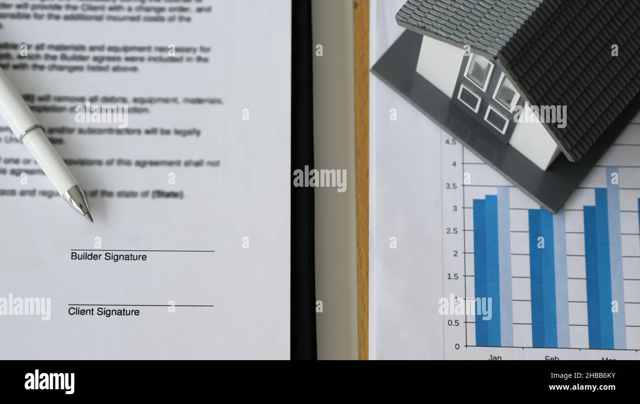 Pen placed on contract documents and model houses on data graphs ...