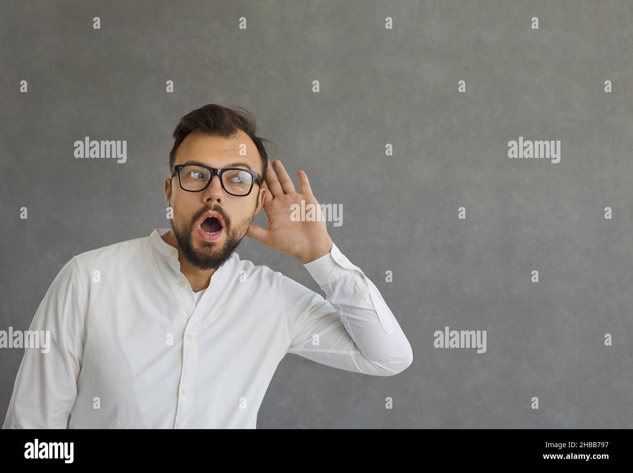 Man with a shocked expression holds his hand to his ear overhearing ...