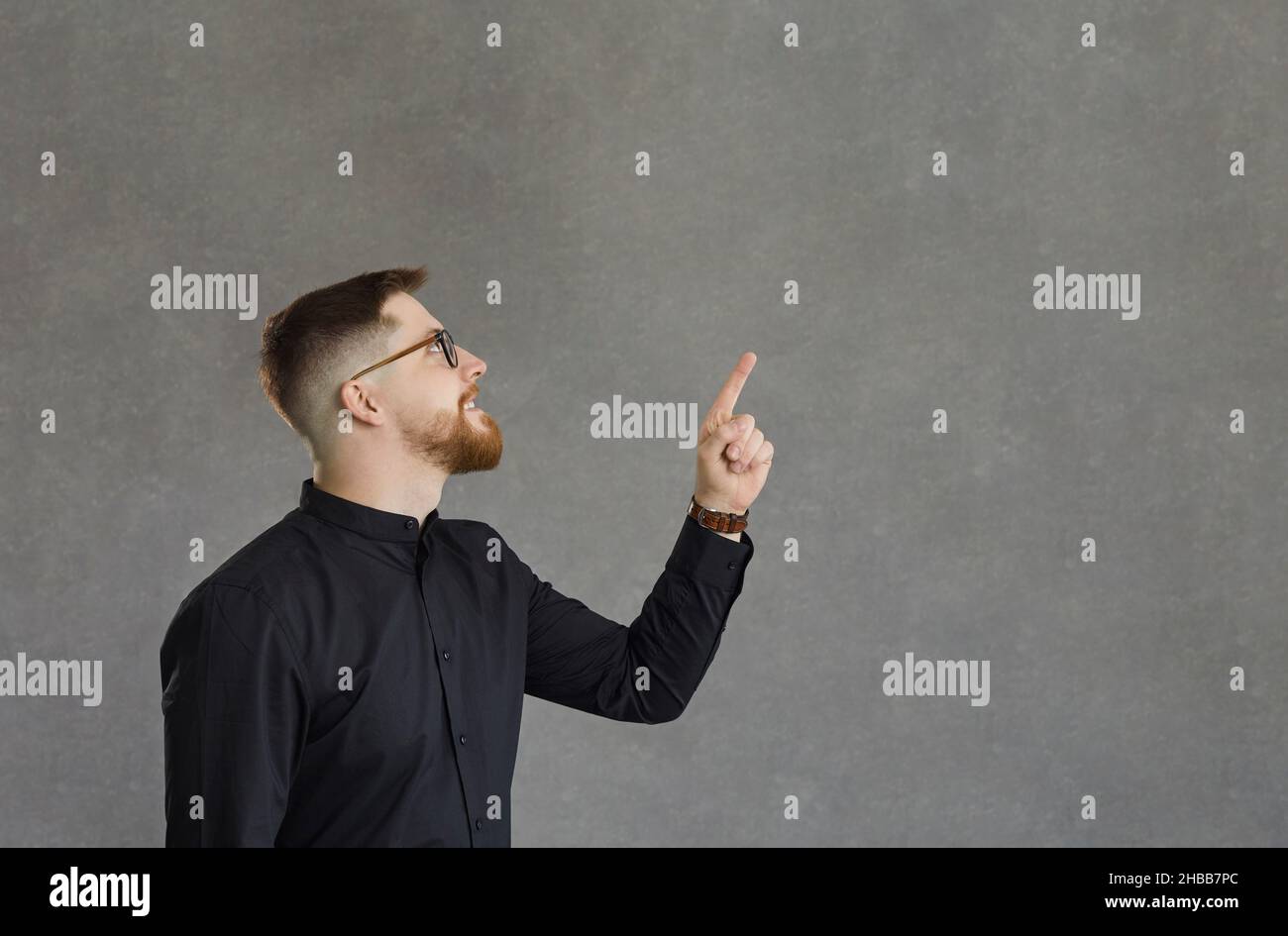 Profile view of a young smiling man pointing his index finger ...