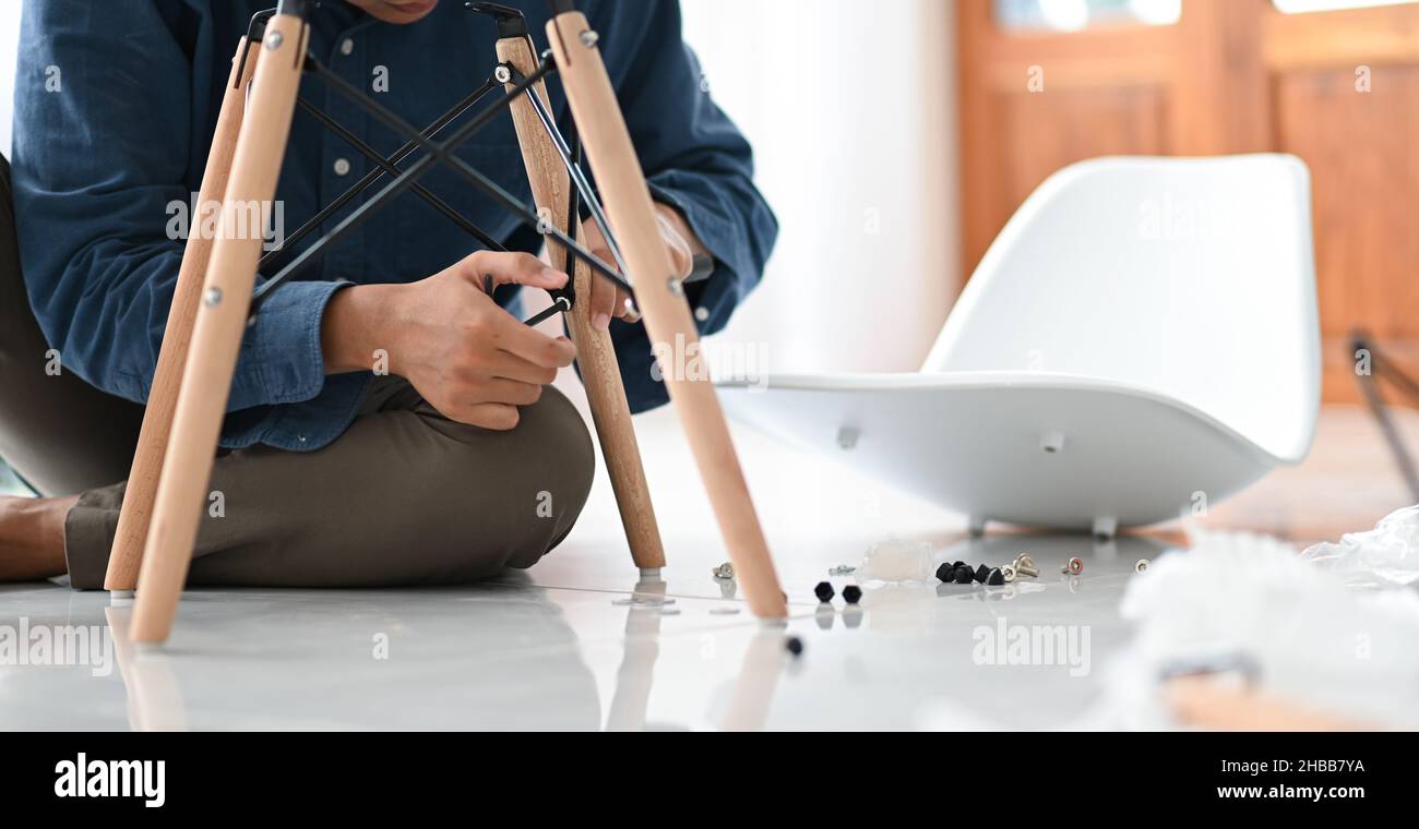 A young man assembling a chair in the house, D.I.Y Repair the chair for ...