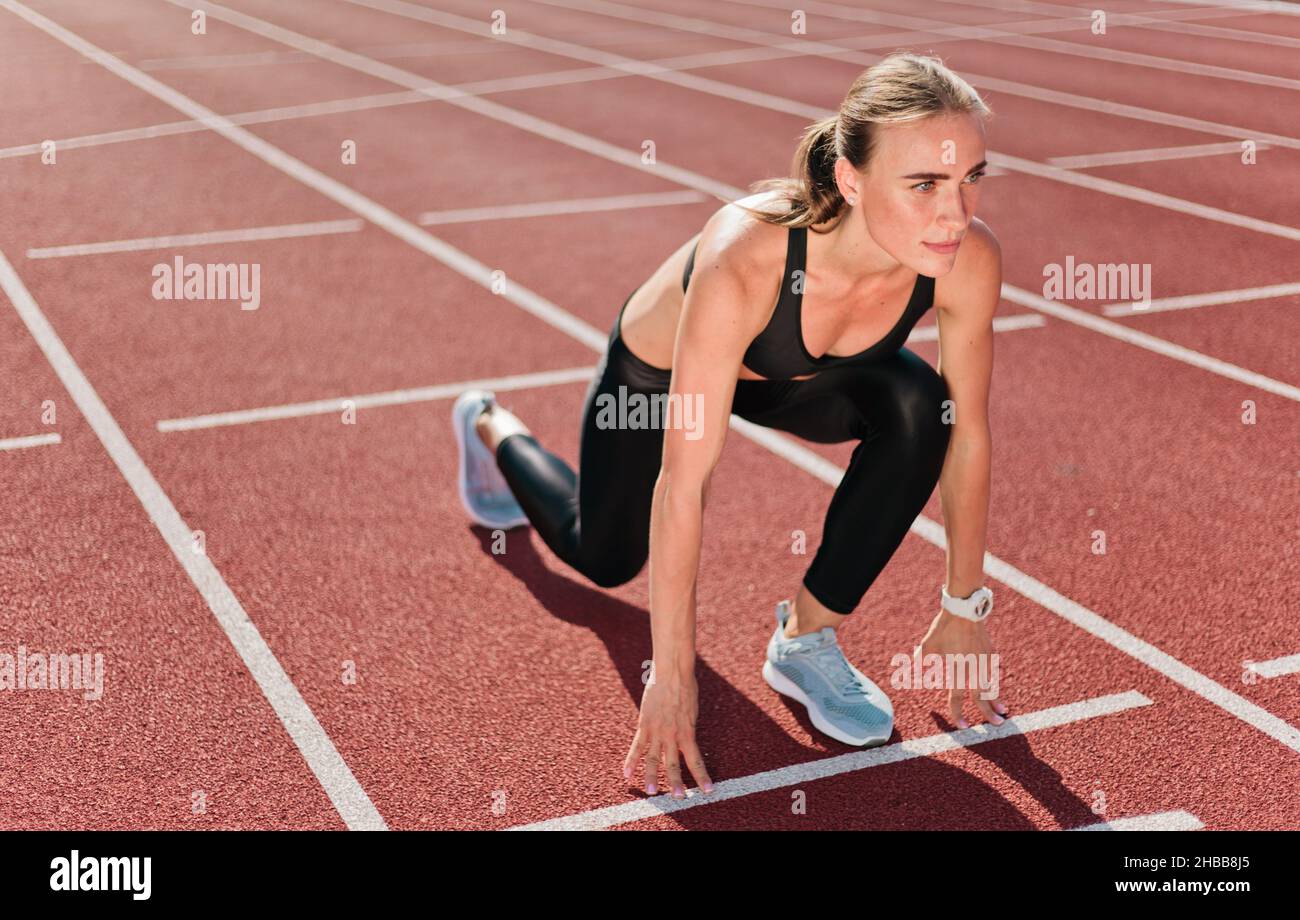 Young motivated woman runner in sportwear getting ready to run sprint ...