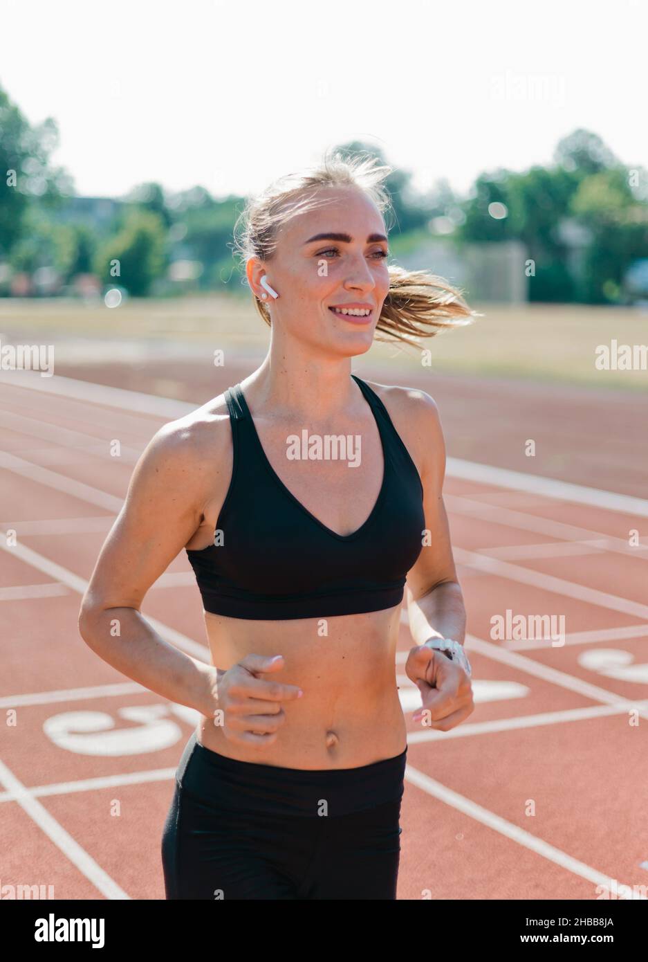 Young cheerful woman runner in sportswear running on stadium track with ...