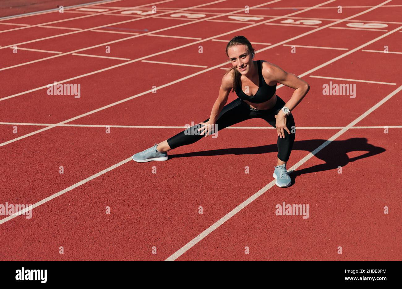 Fit woman in sportswear doing warm-up before jogging on stadium track ...