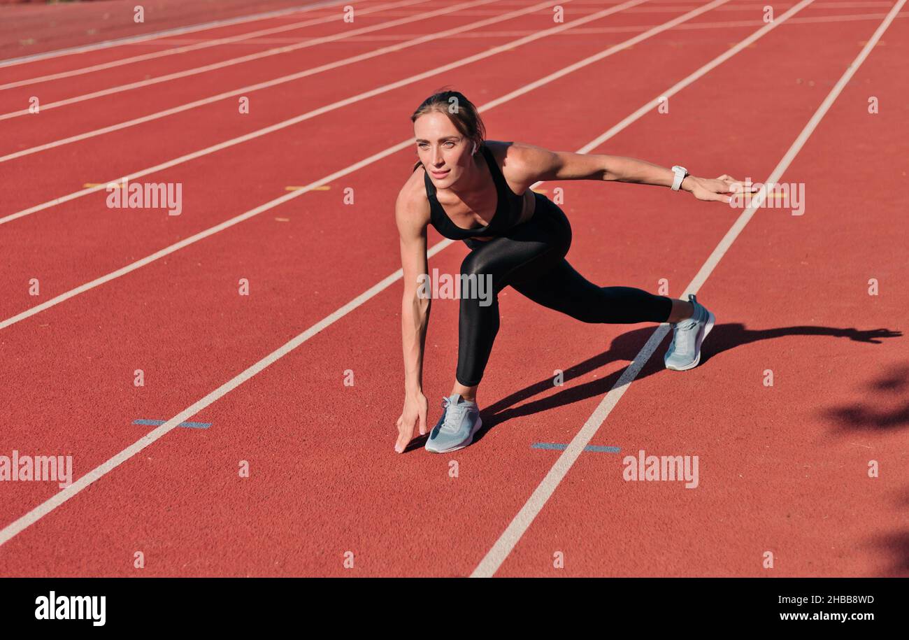 Fit woman in sportswear doing warm-up before jogging on stadium track ...