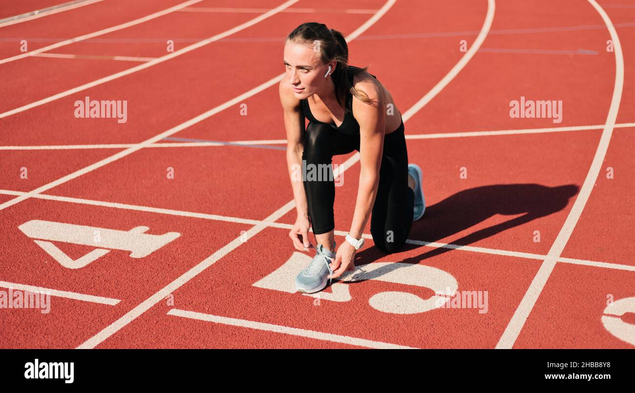 Young sprinter woman in sportswear tying shoelaces before a race on a ...