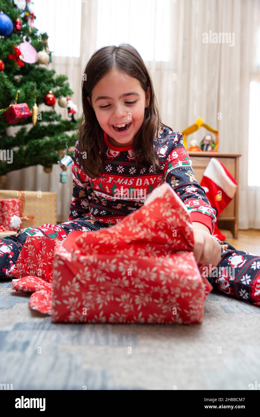 Very happy little Caucasian girl opening Christmas presents at home ...