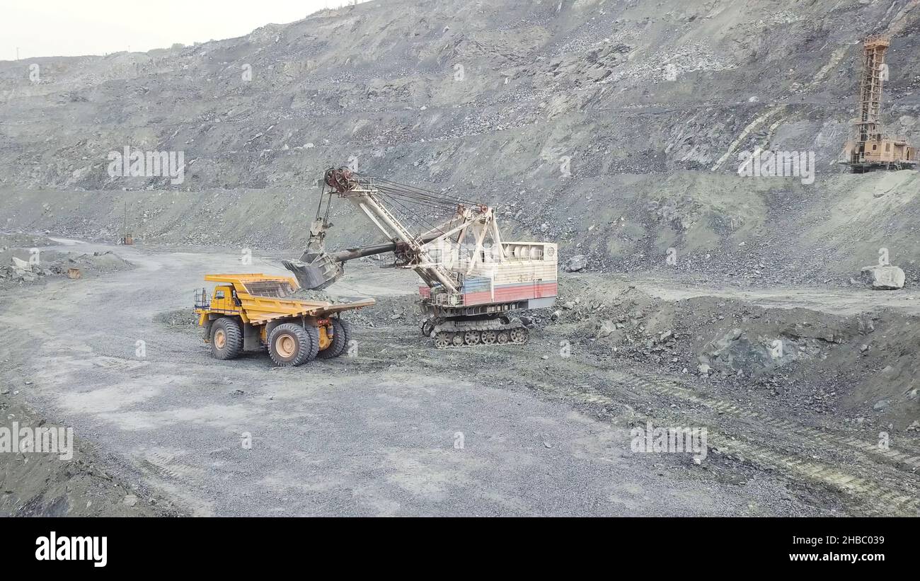 Excavator and dump truck while loading stone ore in a grey quarry ...