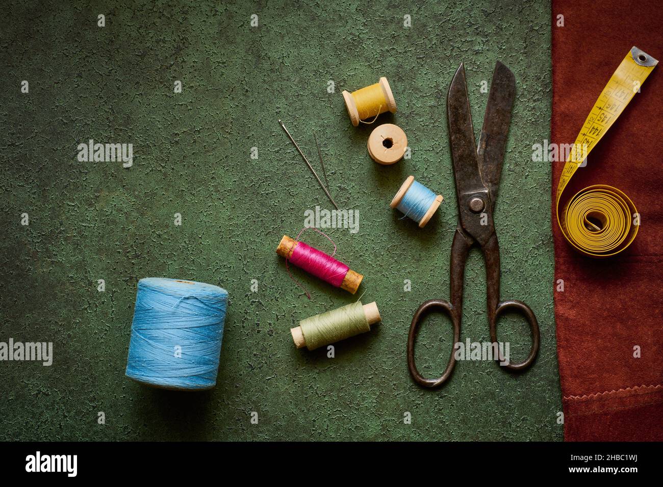 Old scissors, tailor tape and spools of thread on a dark green textured ...
