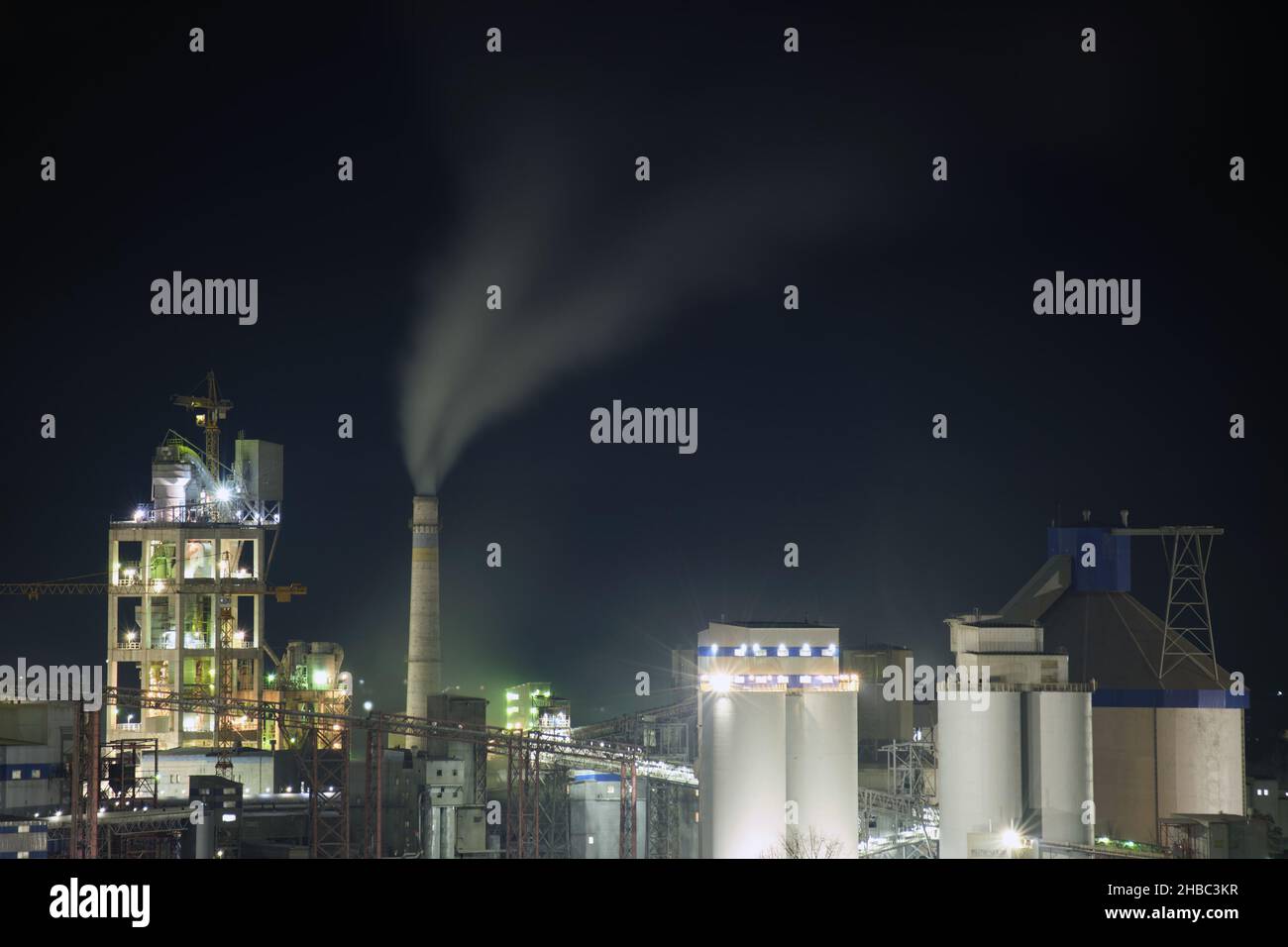 Illuminated cement plant with high factory structure and tower cranes ...
