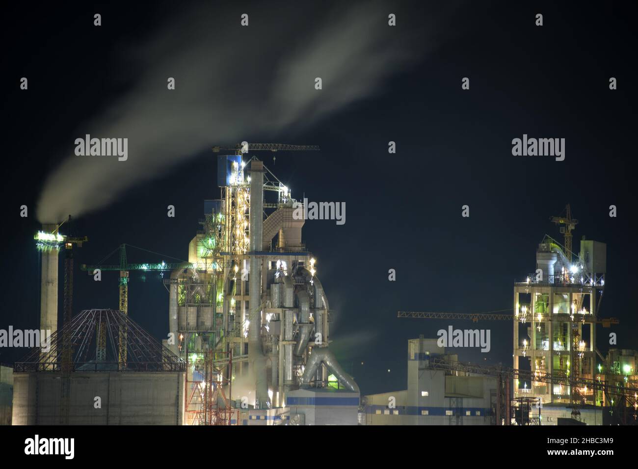 Illuminated cement plant with high factory structure and tower cranes ...