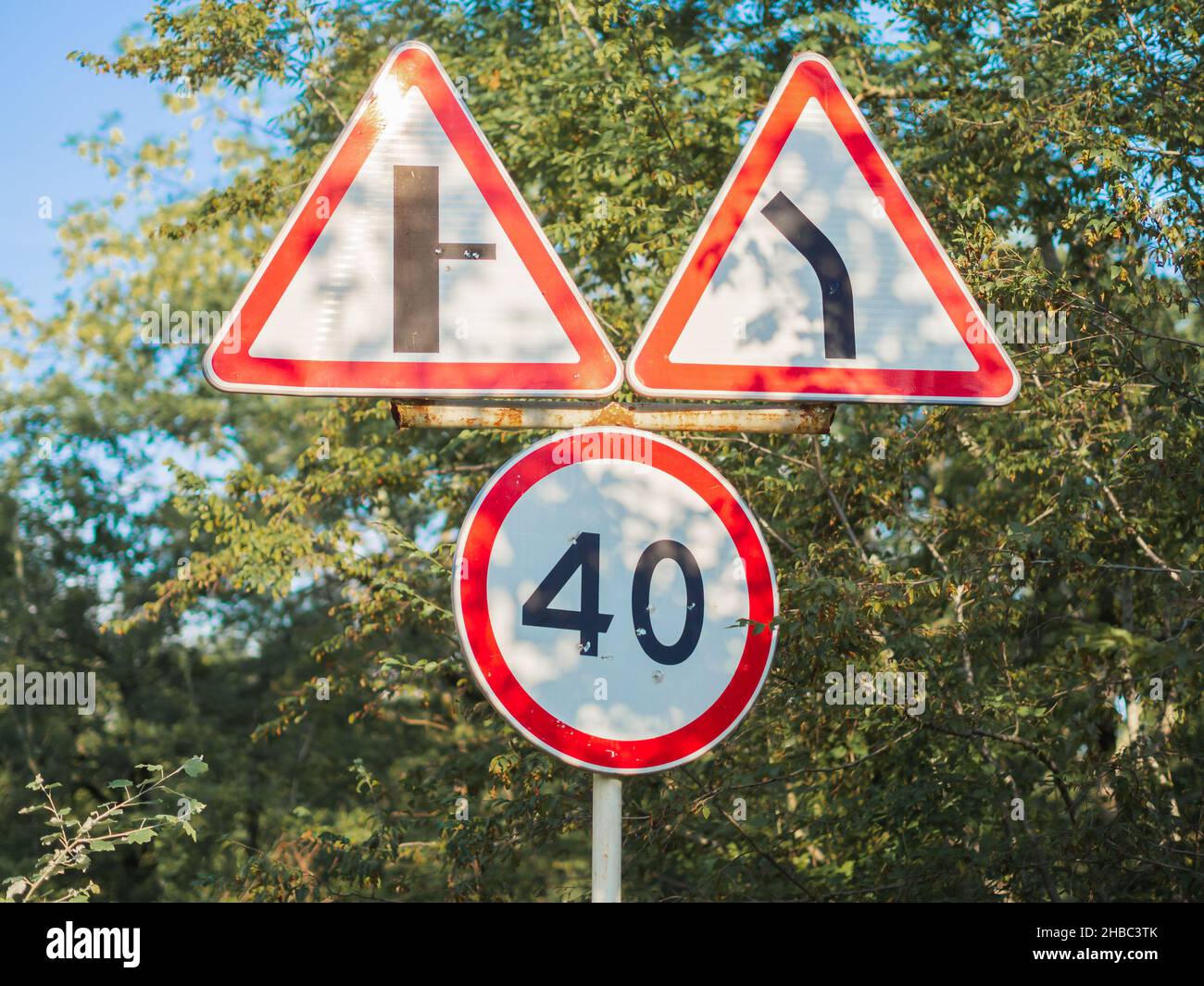 Triple road sign signifying speed limit and turning against green trees ...