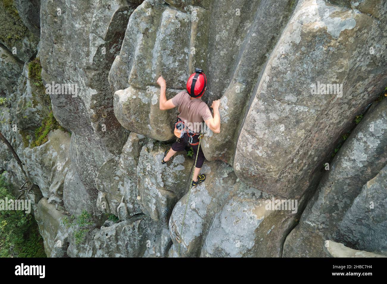 Young man climbing steep wall of rocky mountain. Male climber overcomes ...