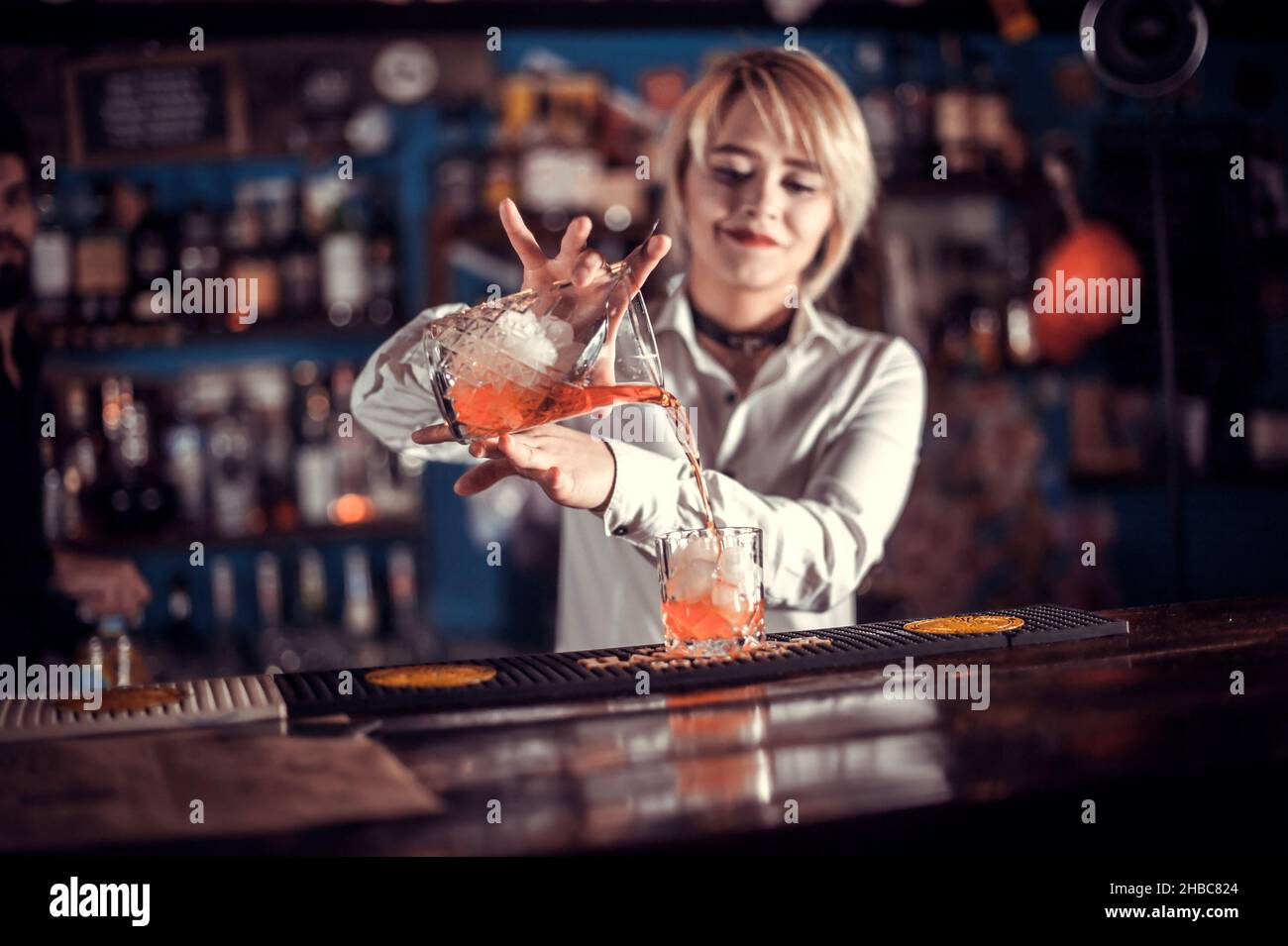 Pretty girl barman demonstrates his skills over the counter at the bar ...