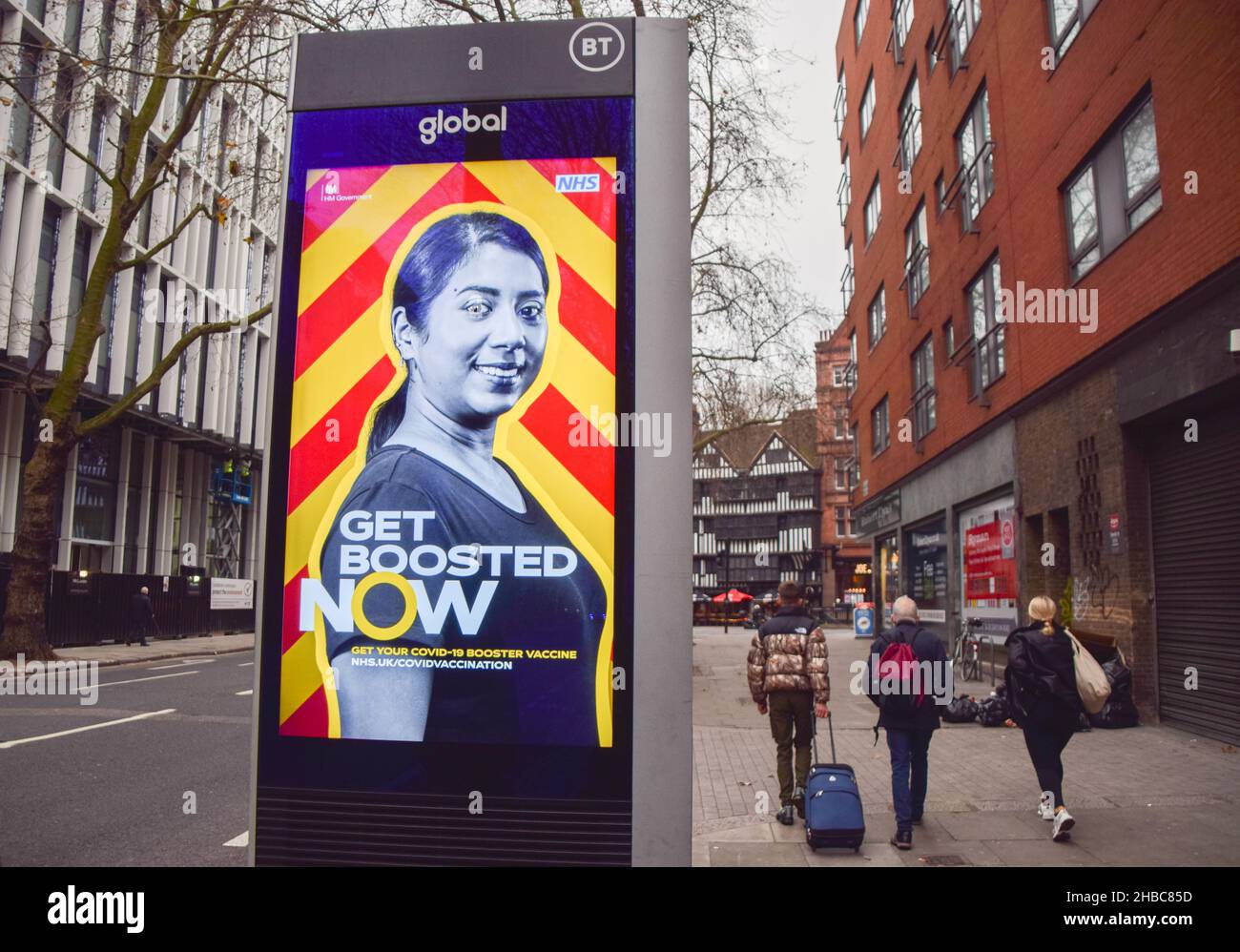 London, UK. 18th Dec, 2021. People walk past an electronic screen ...
