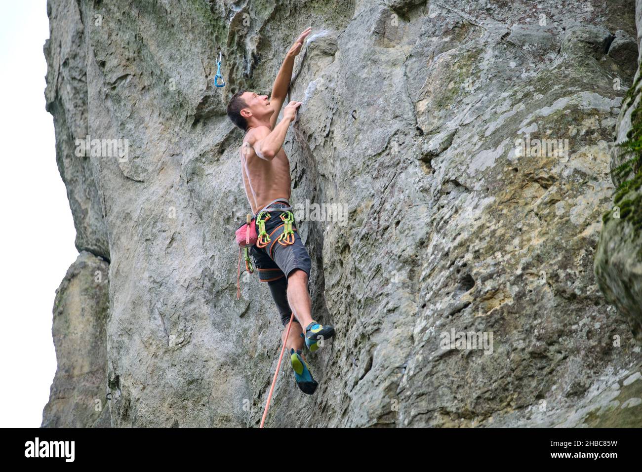 Young man climbing steep wall of rocky mountain. Male climber overcomes ...