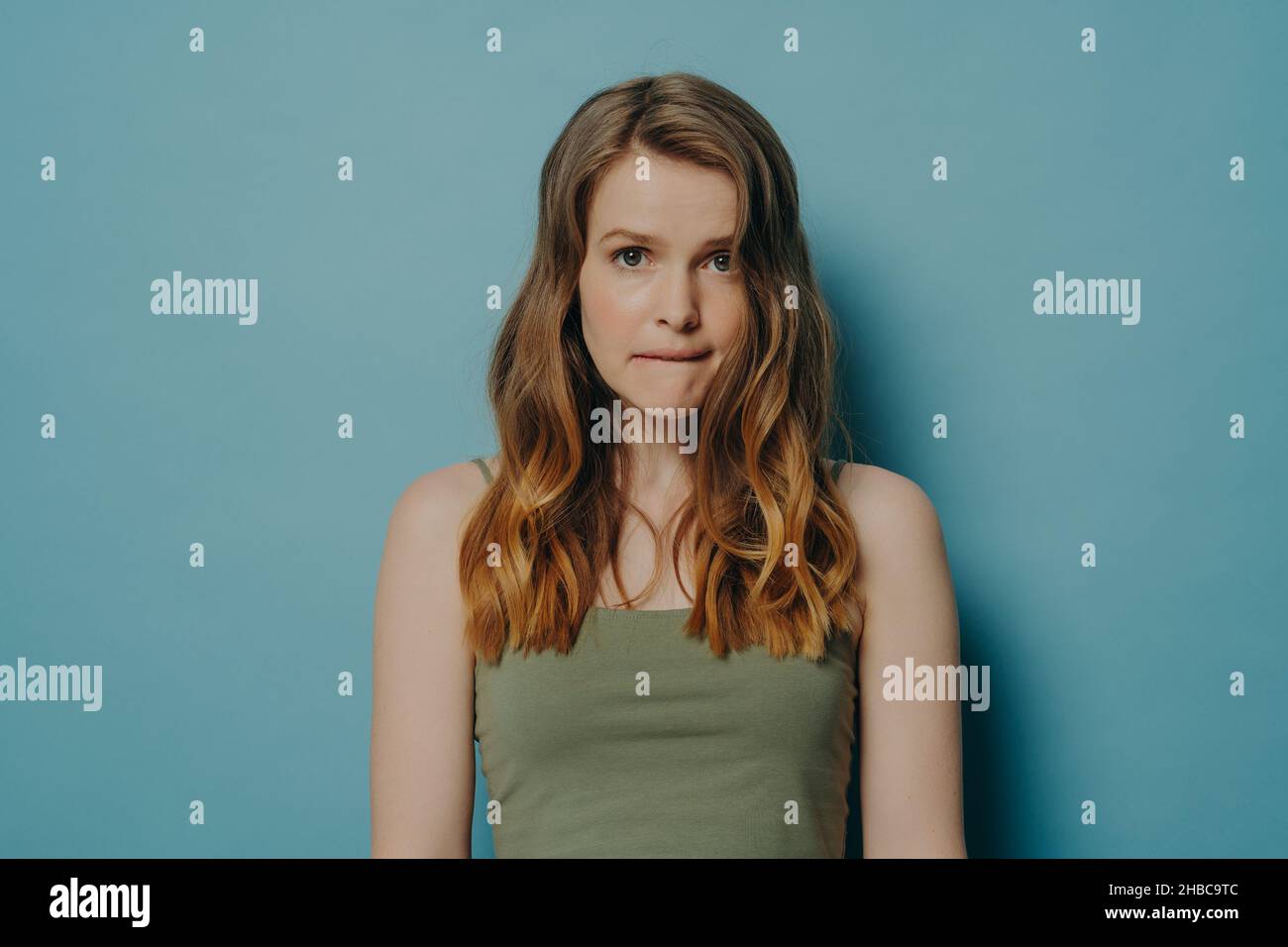 Confused worried young woman with wavy hair biting lip and feeling ...