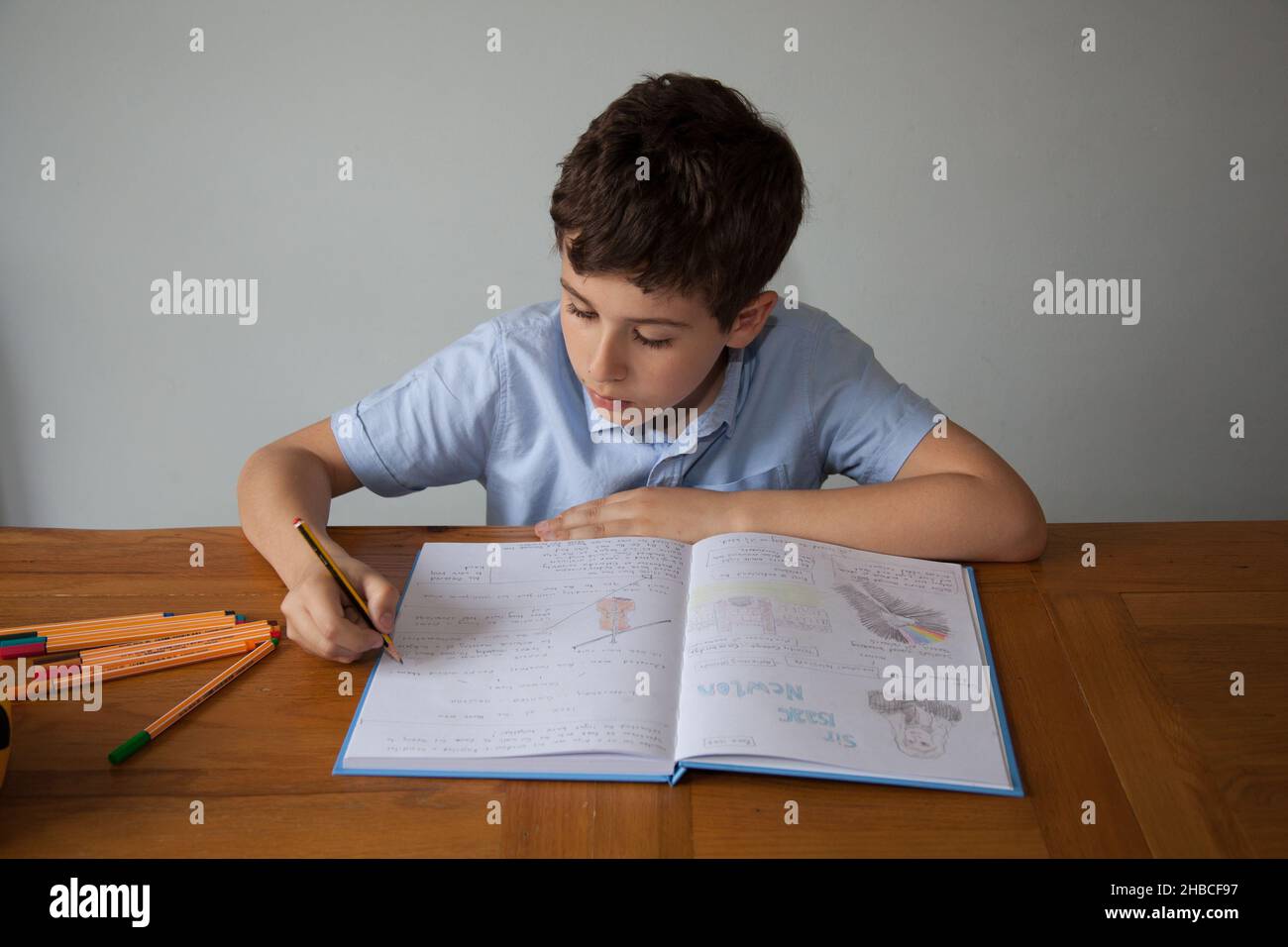 A school boy, aged 11 doing some homework with an open work book ...