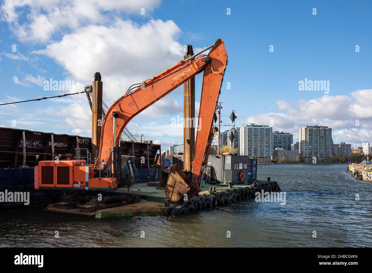 Excavator on a barge, Merihaka district in the background, in ...