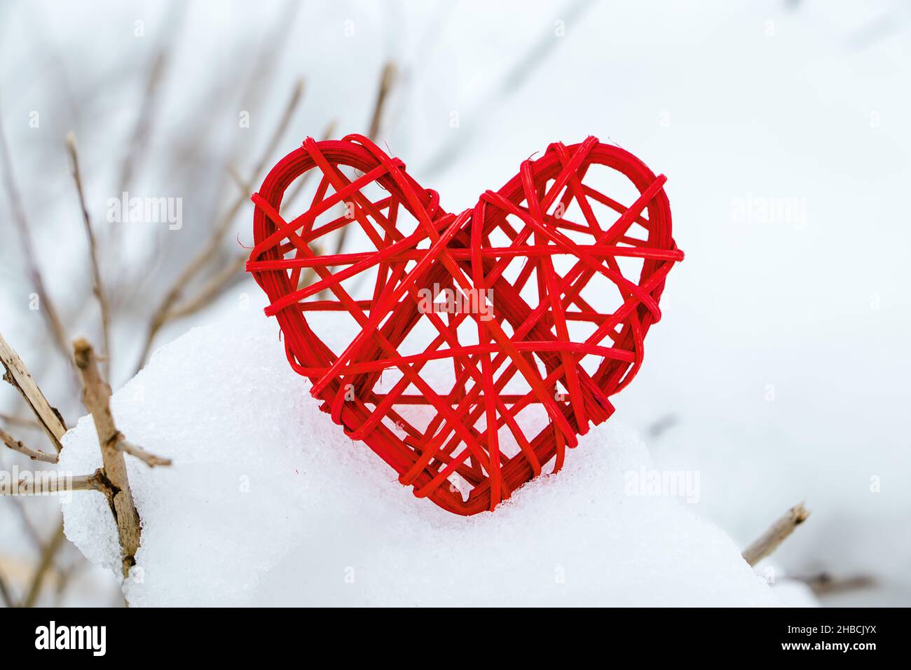 Wooden red heart on background of snow-covered tree branches. Eco ...