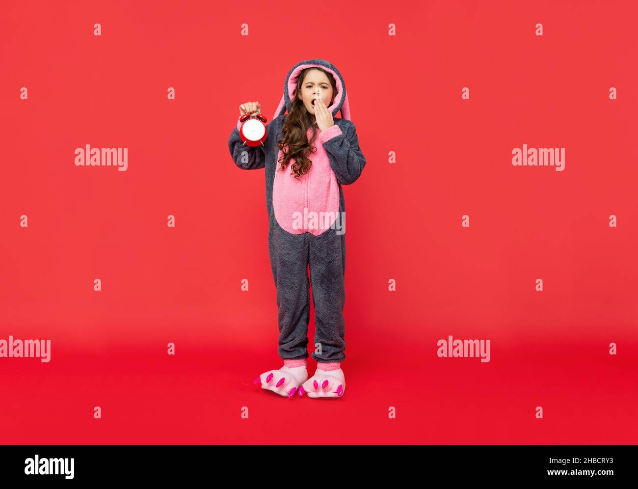 sleepy yawning teen girl in soft night suit hold alarm clock on red ...