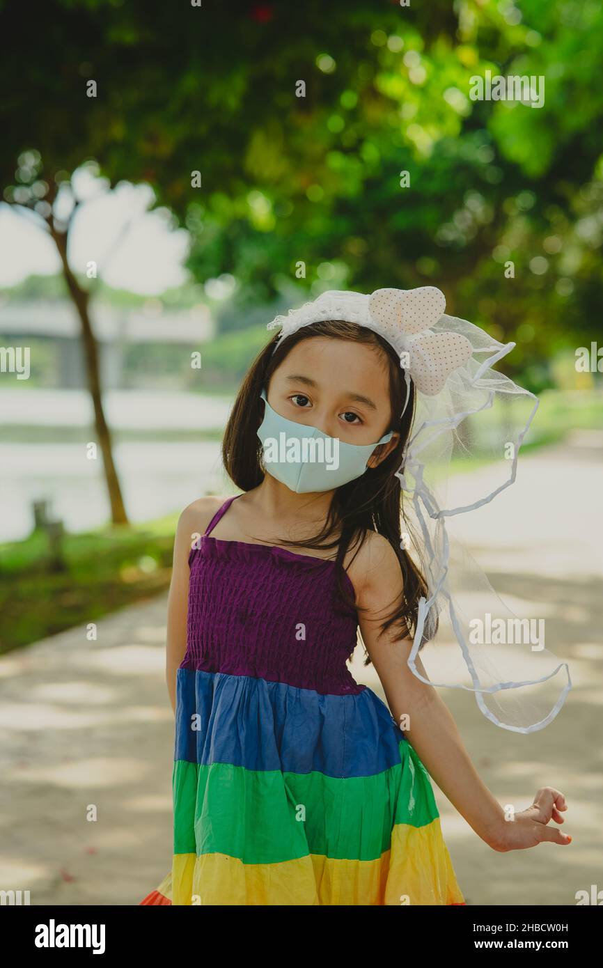 Little girl wearing face mask with rainbow dress enjoying outdoor in ...