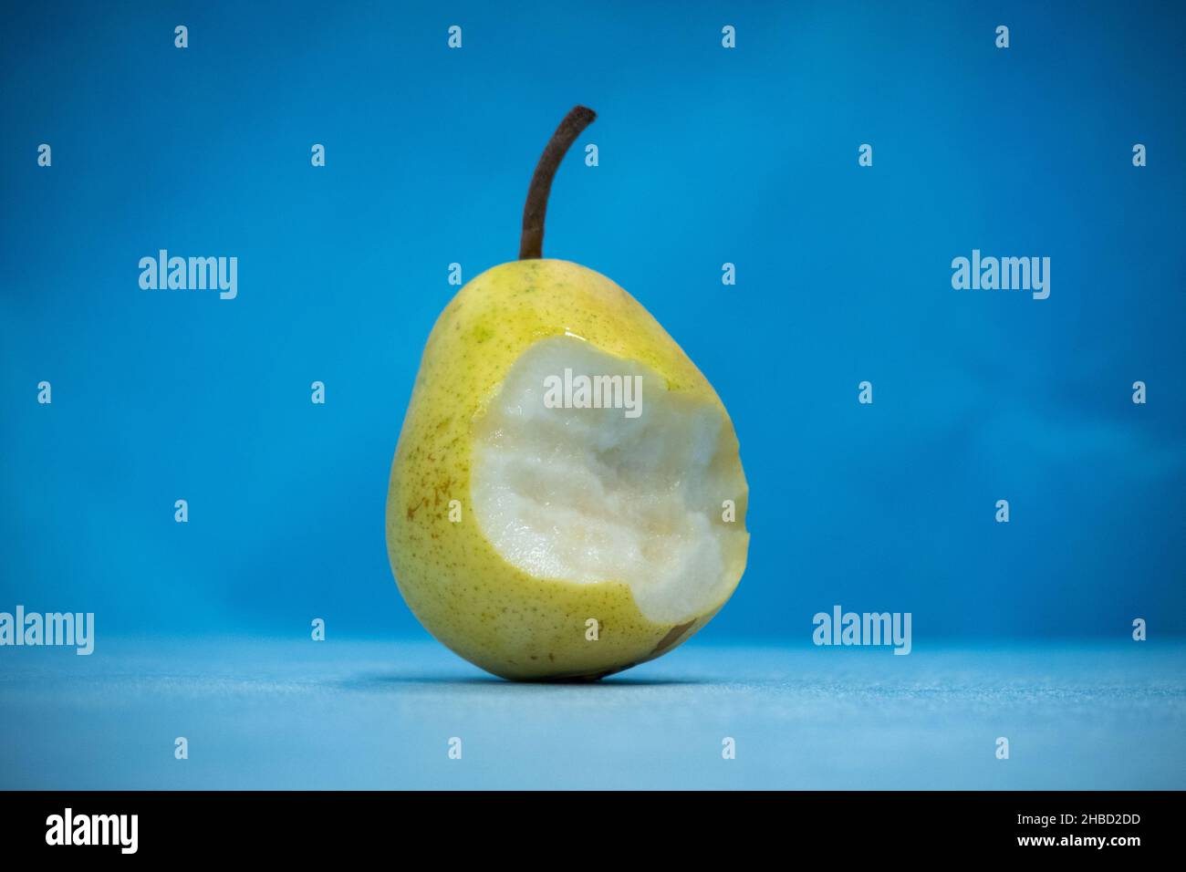 a close up of a bitten pear is standing and the background is blue ...