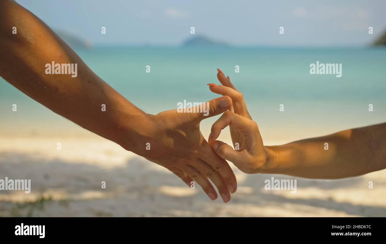Hands of flirting young man and woman touching on beach in palms shadow ...