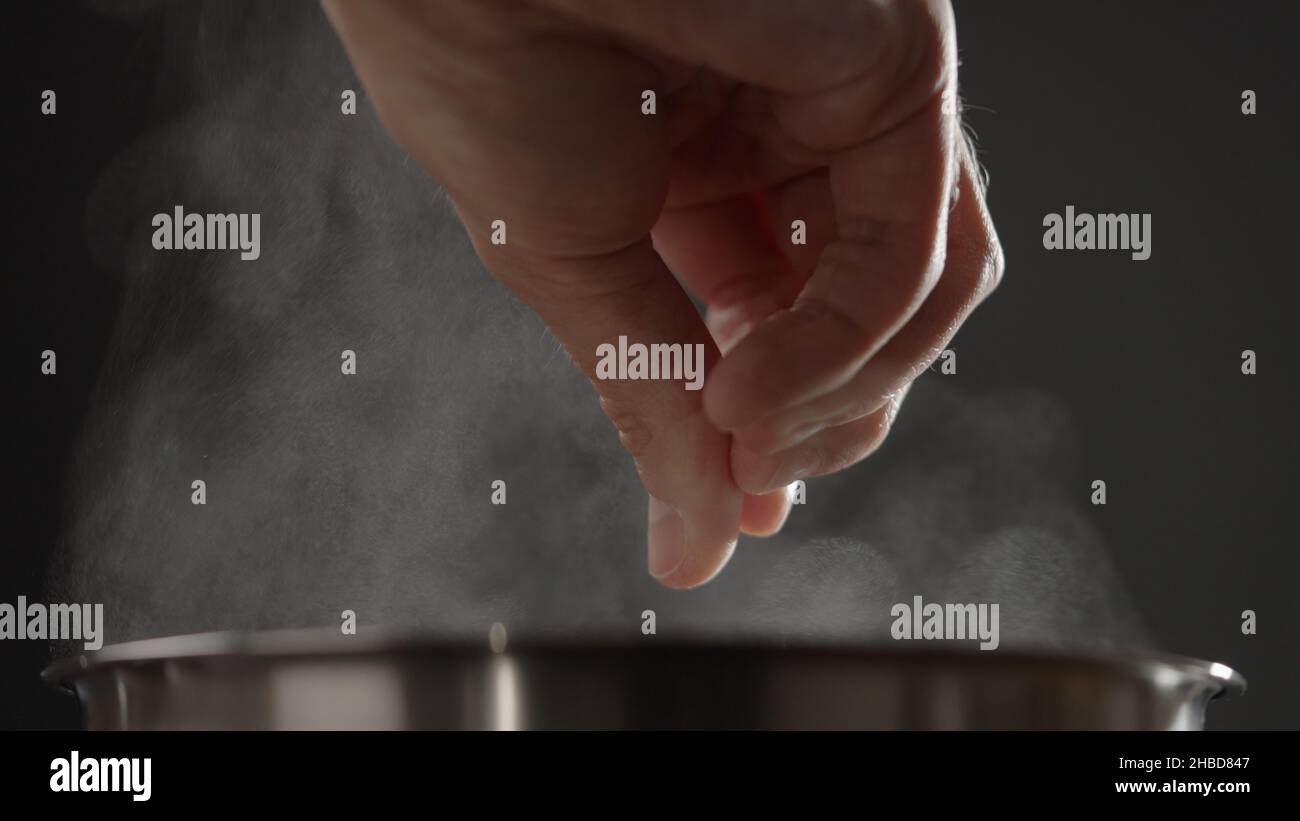 man adding salt to boiling water in saucepan with strong backlight ...