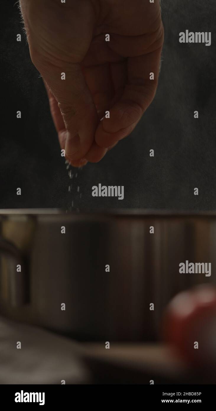 vertical shot man adding salt to boiling water in saucepan, vertical ...