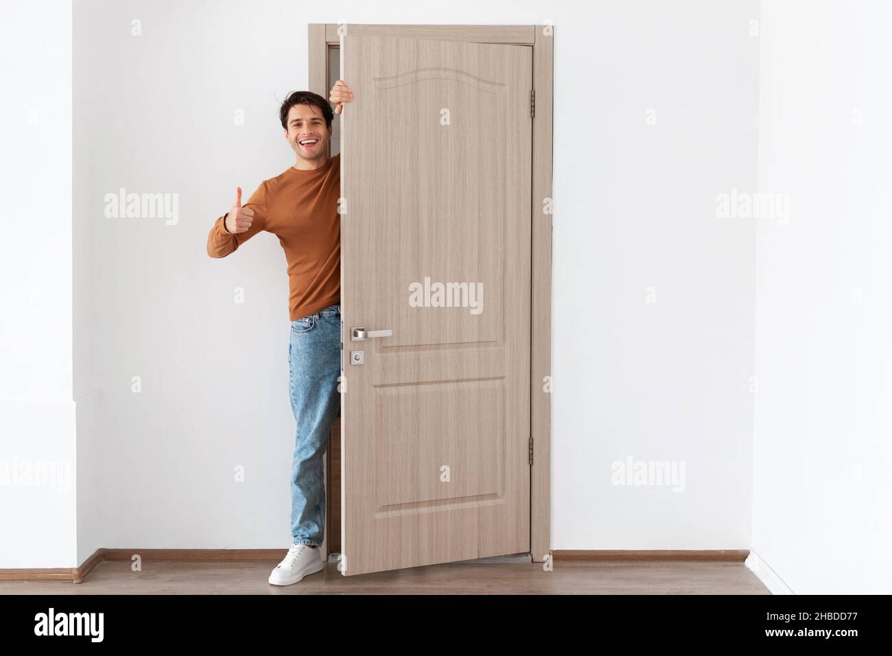Cheerful guy looking out of door showing thumb up gesture Stock Photo ...
