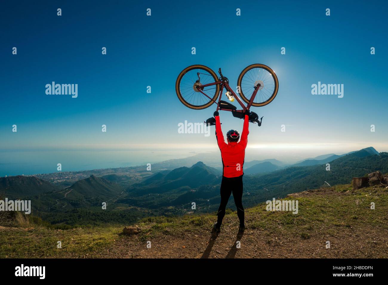 Successful adult male cyclist rises his bicycle over his head on top of ...