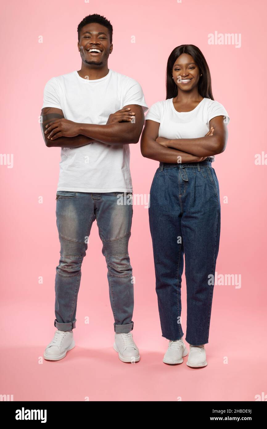 Confident couple standing with folded arms at pink studio background ...