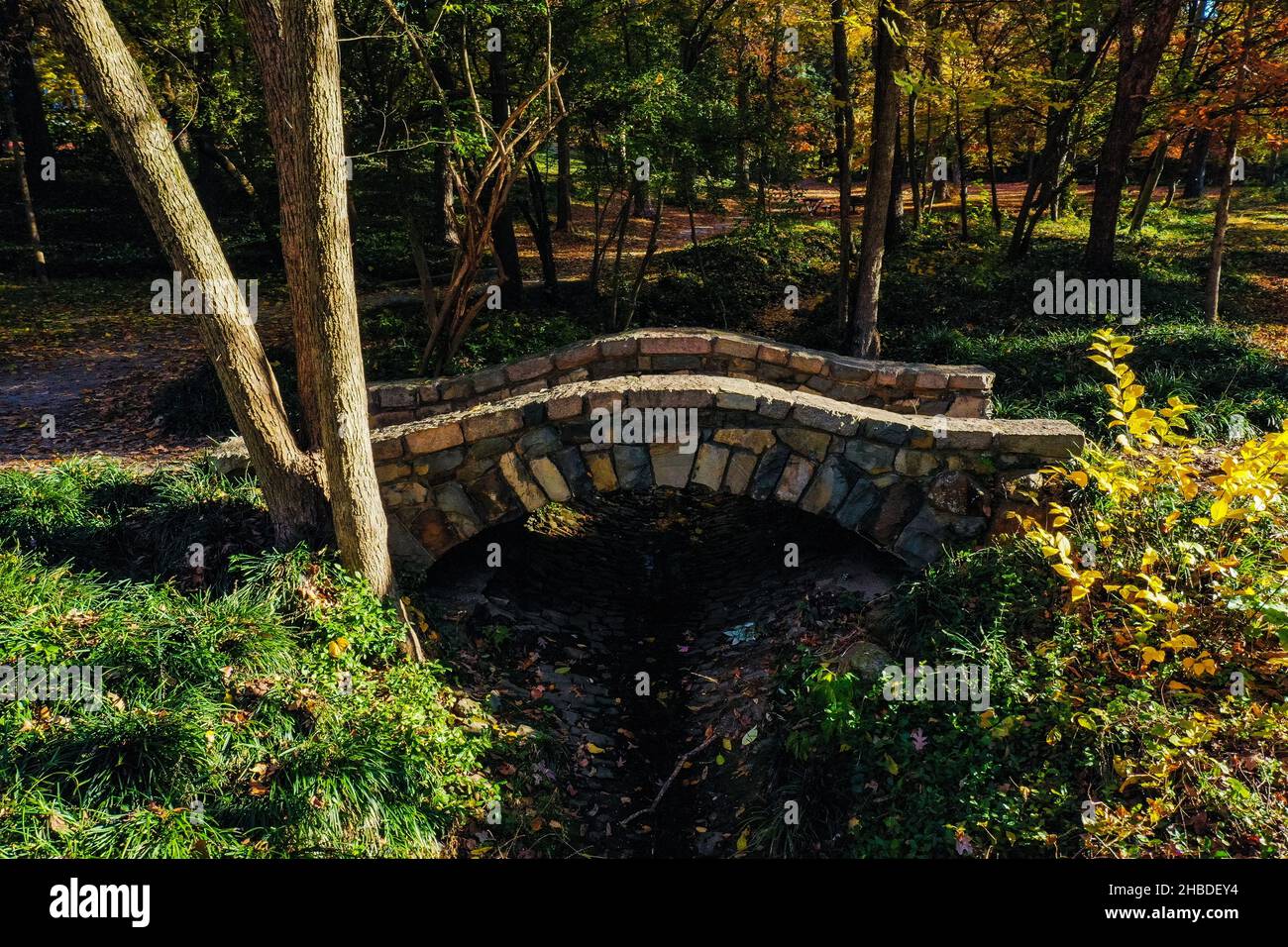A view of a stone walking path bridge in the park with green trees on a ...