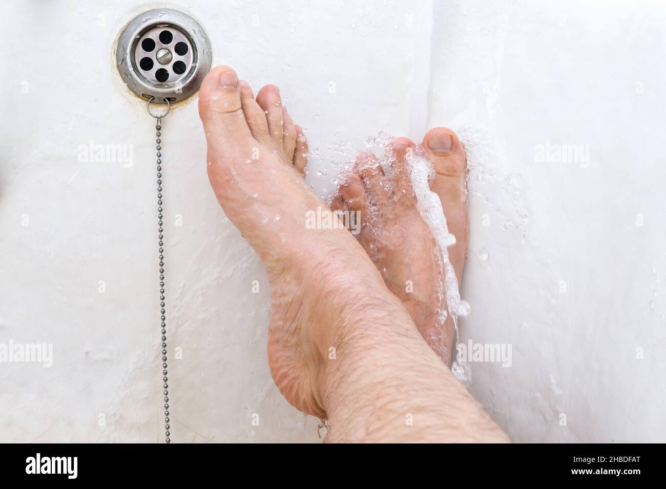Man relaxes in the bathroom washing his feet under a tap of hot water ...