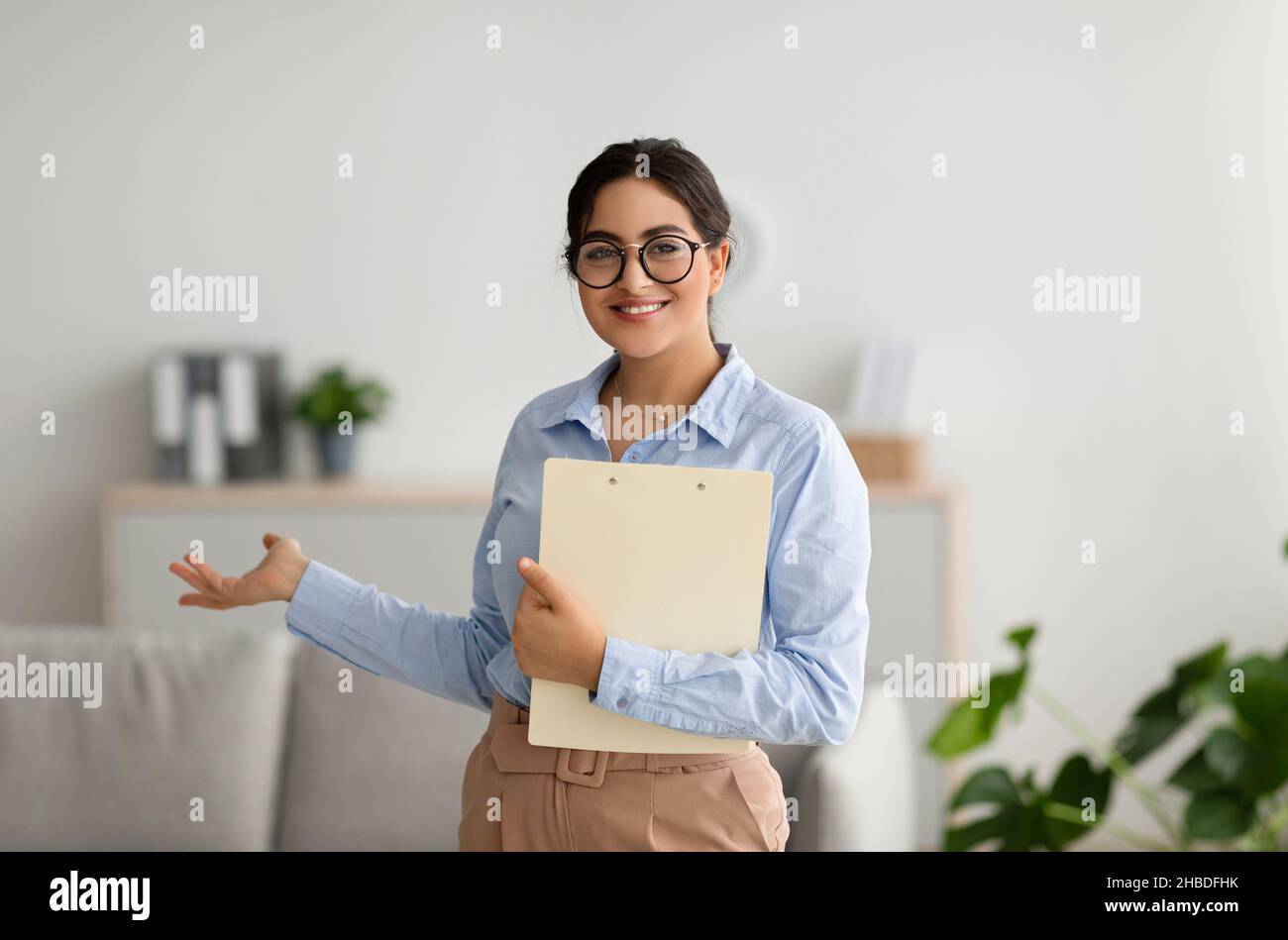 Cheerful arab female psychologist with clipboard showing something with ...