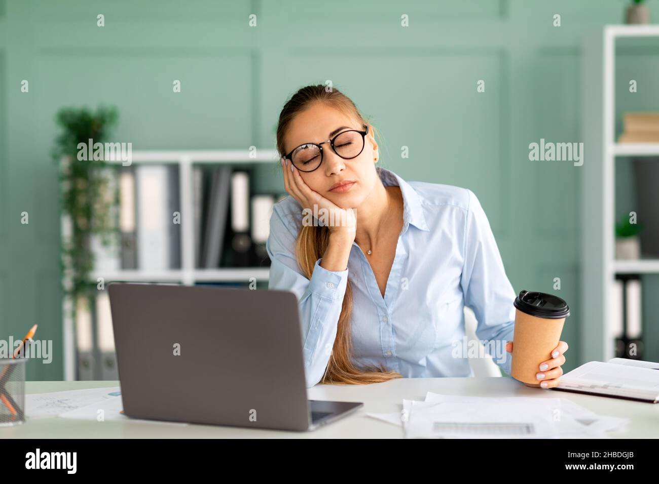 Young businessman tired of computer work sleeping at workplace, holding ...