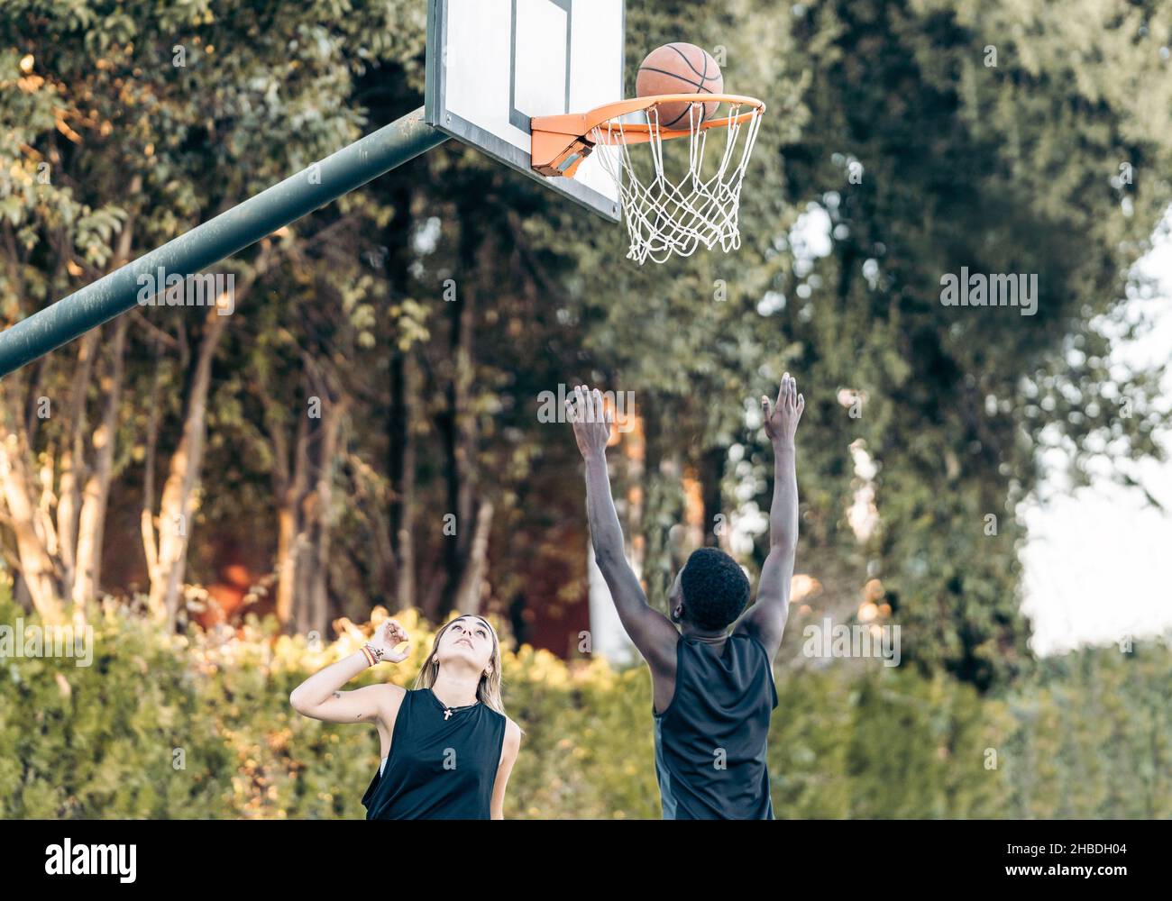 Ball going into a basketball basket while some multiethnic friends are ...