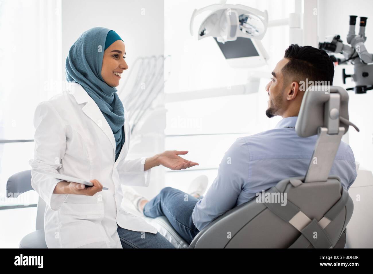 Muslim Dentist Woman With Digital Tablet Consulting Male Patient About ...