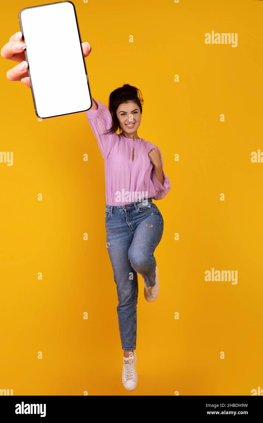 Excited armenian woman holding smartphone, showing blank screen ...