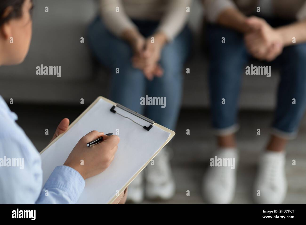 Marital counselor taking notes at therapy session with young spouses ...