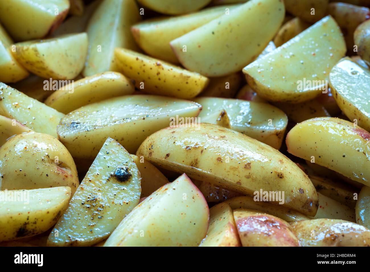 fresh raw potatoes wedges mixed with oil and spices ready for baking ...