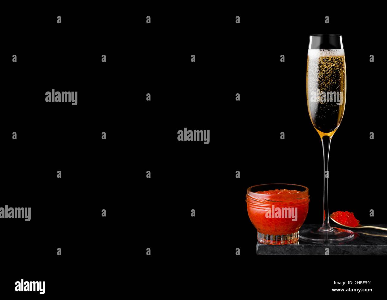 Elegant glass of yellow champagne with red caviar on golden spoon and ...