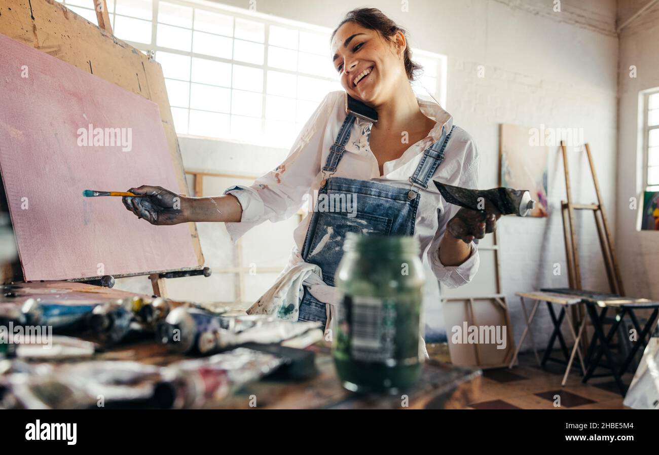 Freelance painter taking a phone call while painting on a canvas in her ...