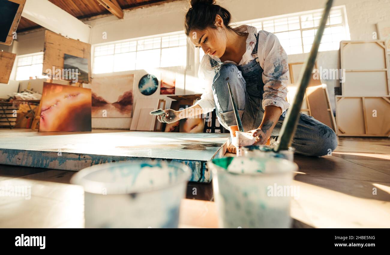 Artist looking at her artwork while painting on a large canvas ...